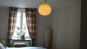 Quarto com cama, janela com cortinas, mesa com abajur e luminária pendente.
