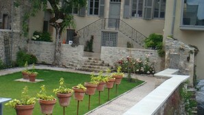 Um pátio com parede de pedra, um pequeno jardim com plantas em vasos e uma escadaria que leva a um edifício.