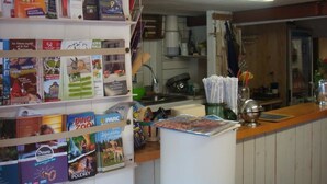 Uma livraria com estantes cheias de livros e revistas, um balcão com um cardápio, e uma área de cozinha ao fundo.