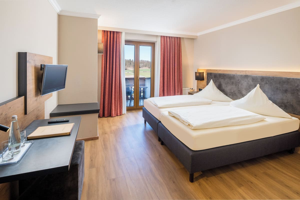 Quarto de hotel com cama, escrivaninha com computador, televisão e vista para o exterior.