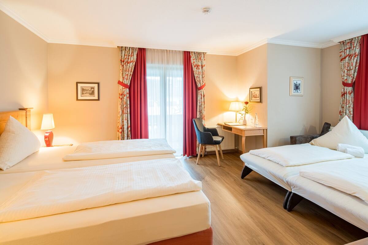 Quarto de hotel com duas camas, uma escrivaninha, uma cadeira e um abajur.
