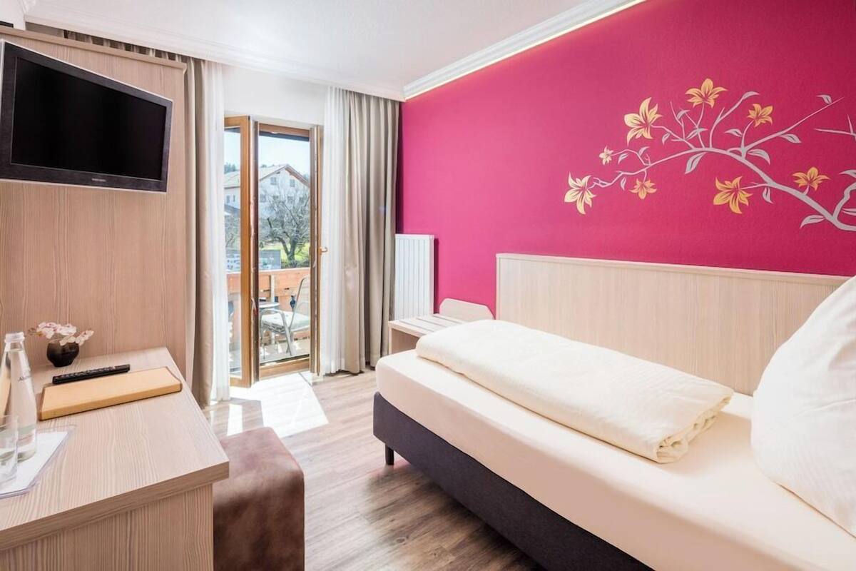 Quarto de hotel com cama, escrivaninha, televisão e vista para o exterior.