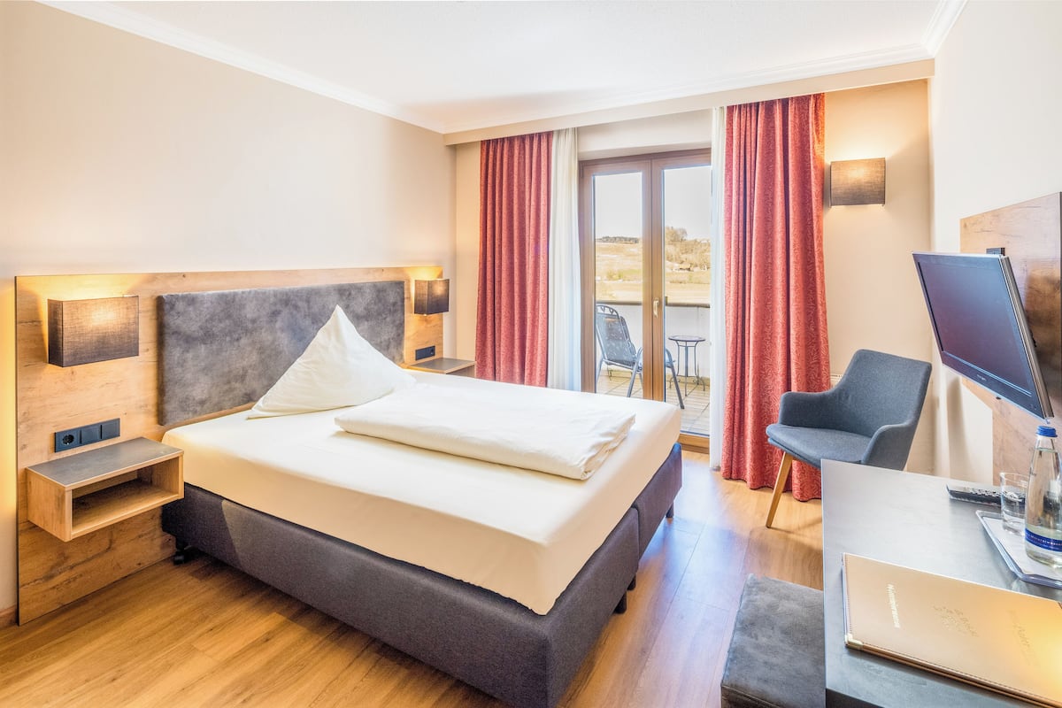 Quarto de hotel com uma cama grande, uma escrivaninha com um laptop, uma cadeira e uma televisão.