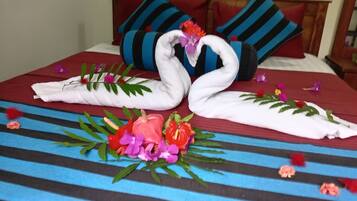Cama com colcha listrada em vermelho e azul, duas toalhas dobradas em formato de cisne e um arranjo floral sobre a cama.
