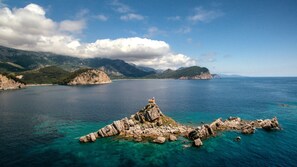 Paisagem costeira com um afloramento rochoso em primeiro plano e montanhas ao fundo.