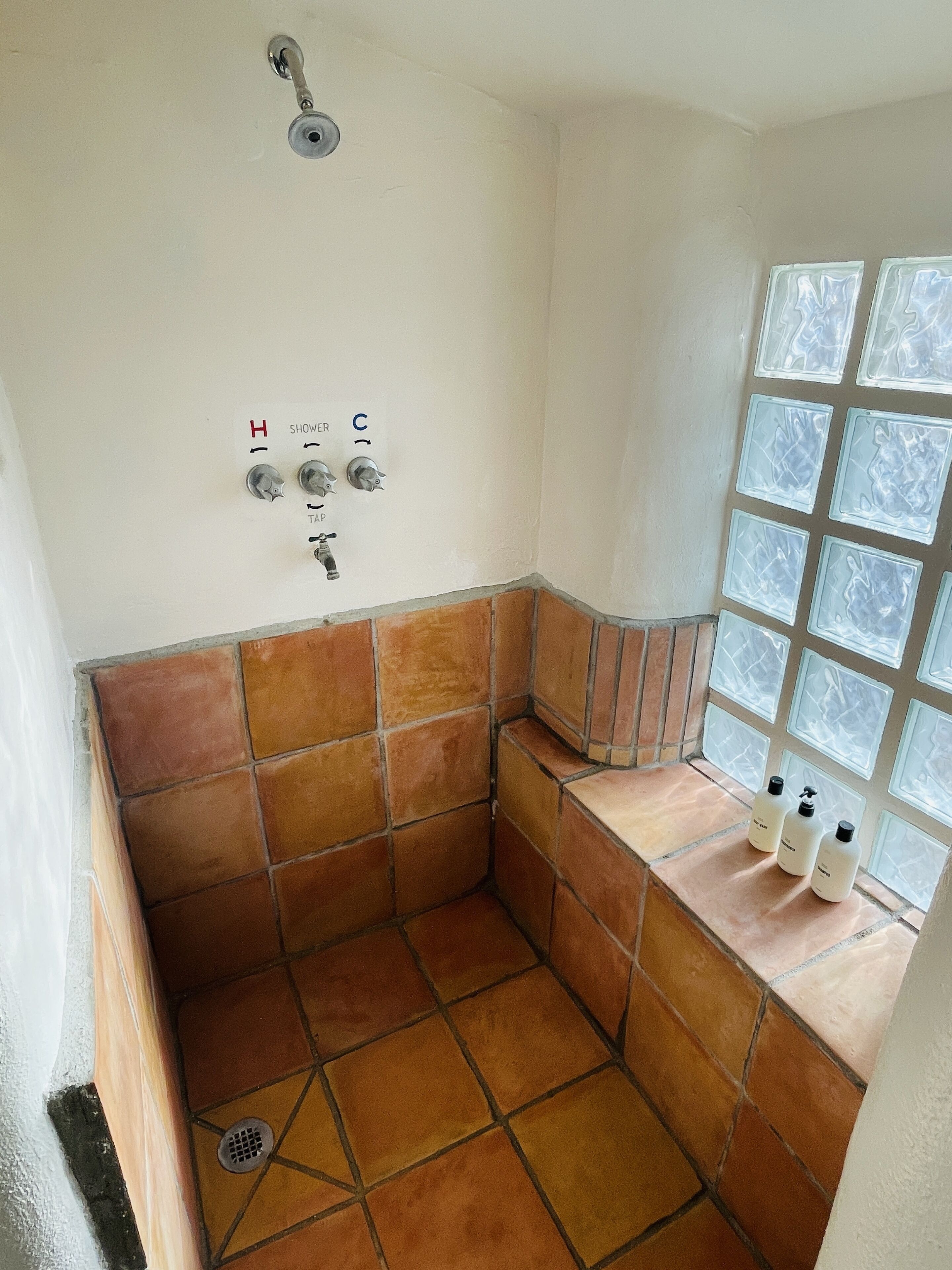 Um espaço de chuveiro pequeno, revestido com azulejos, com uma janela e duas garrafas no parapeito.