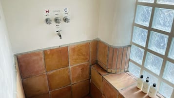 Um espaço de chuveiro pequeno, revestido com azulejos, com uma janela e duas garrafas no parapeito.