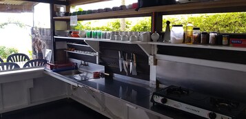 Cozinha com fogão a gás, prateleiras com utensílios de cozinha e janela com vegetação lá fora.