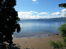 Uma praia com águas calmas, uma cadeia de montanhas ao longe e um céu claro.