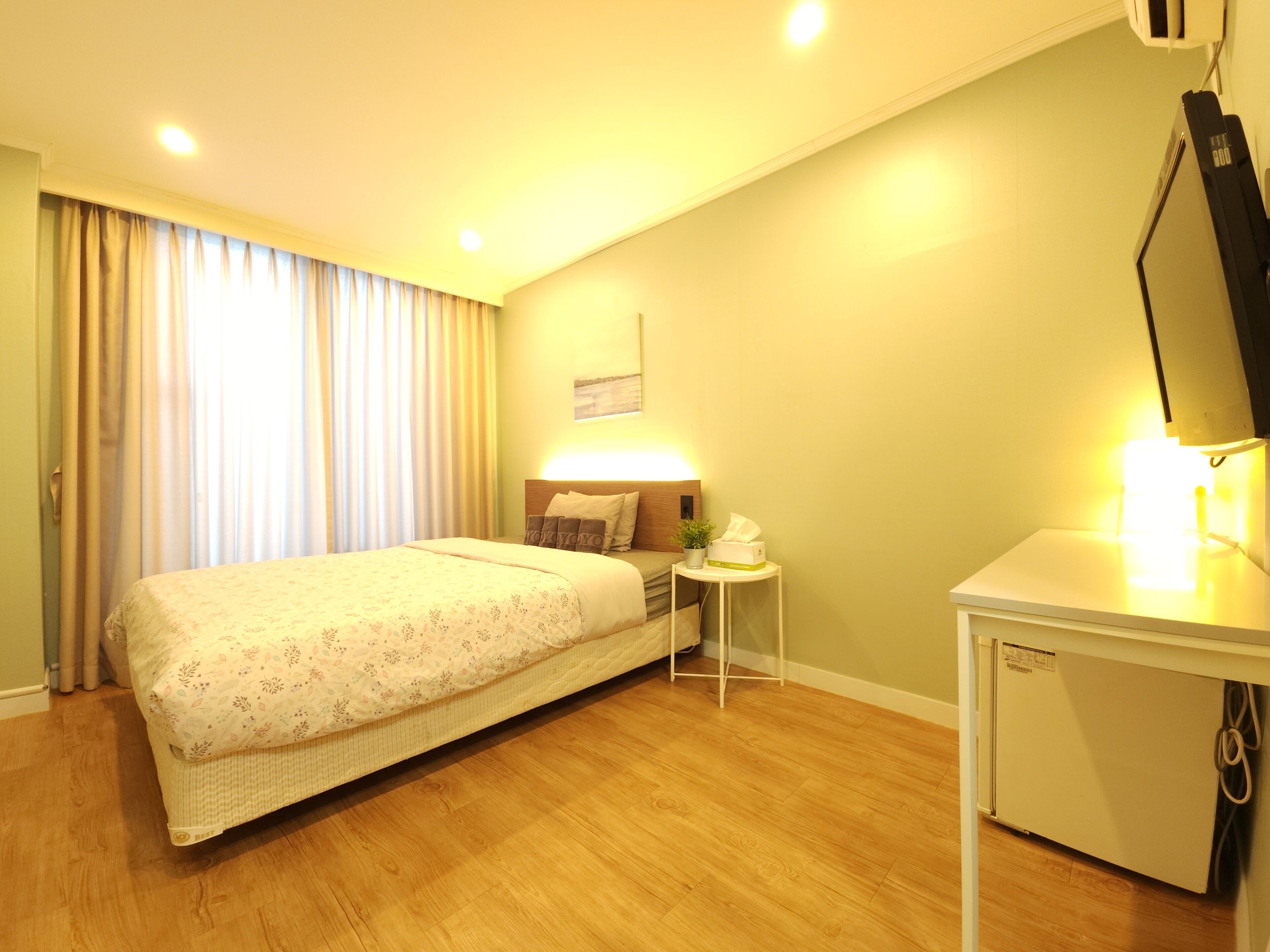 Quarto de hotel com cama, mesa de cabeceira, luminária e pequena escrivaninha com luminária.