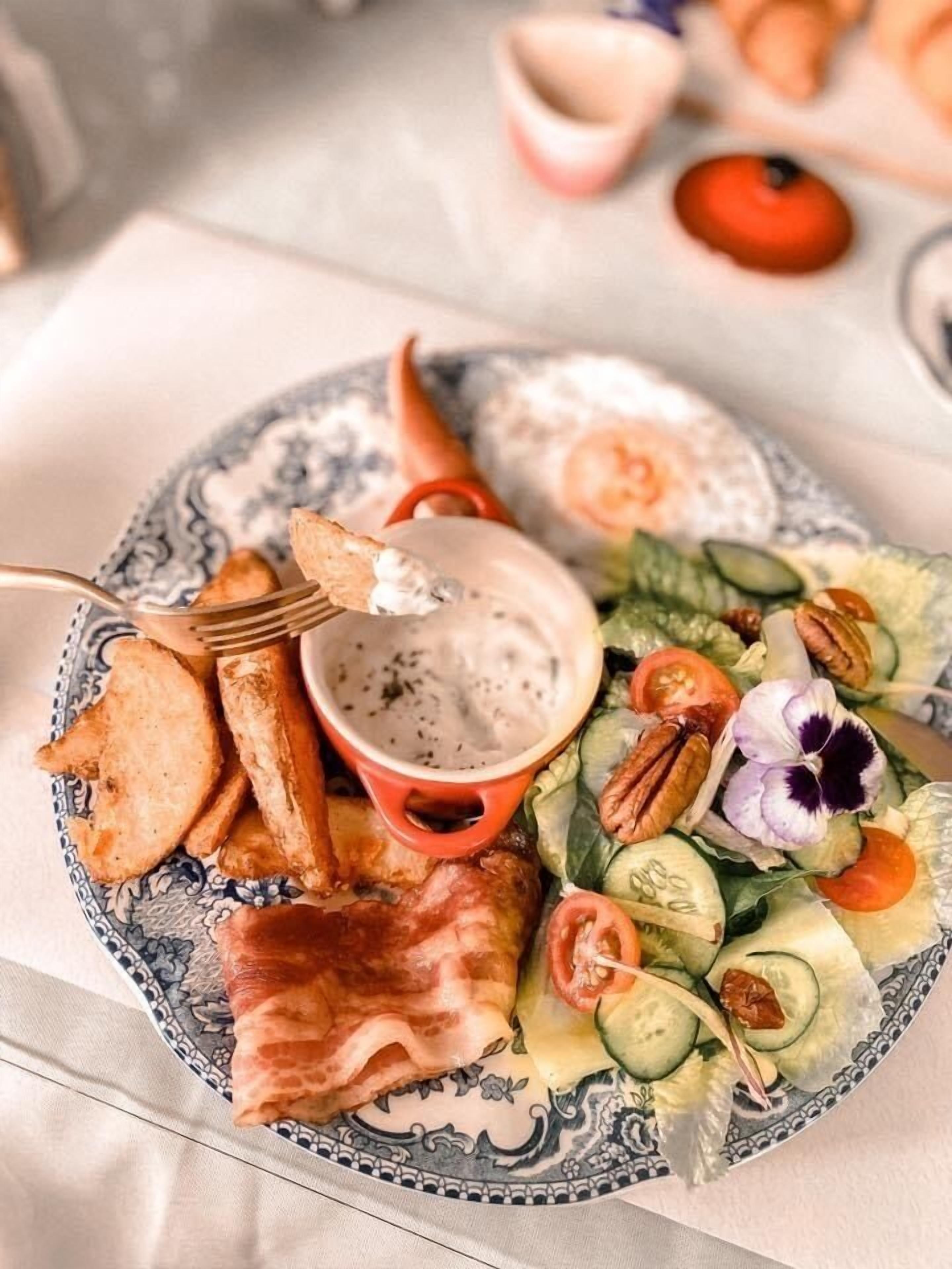 Um prato com itens de café da manhã, incluindo torradas, bacon, uma salada com pepinos, tomates e nozes pecan, e uma xícara de sopa.