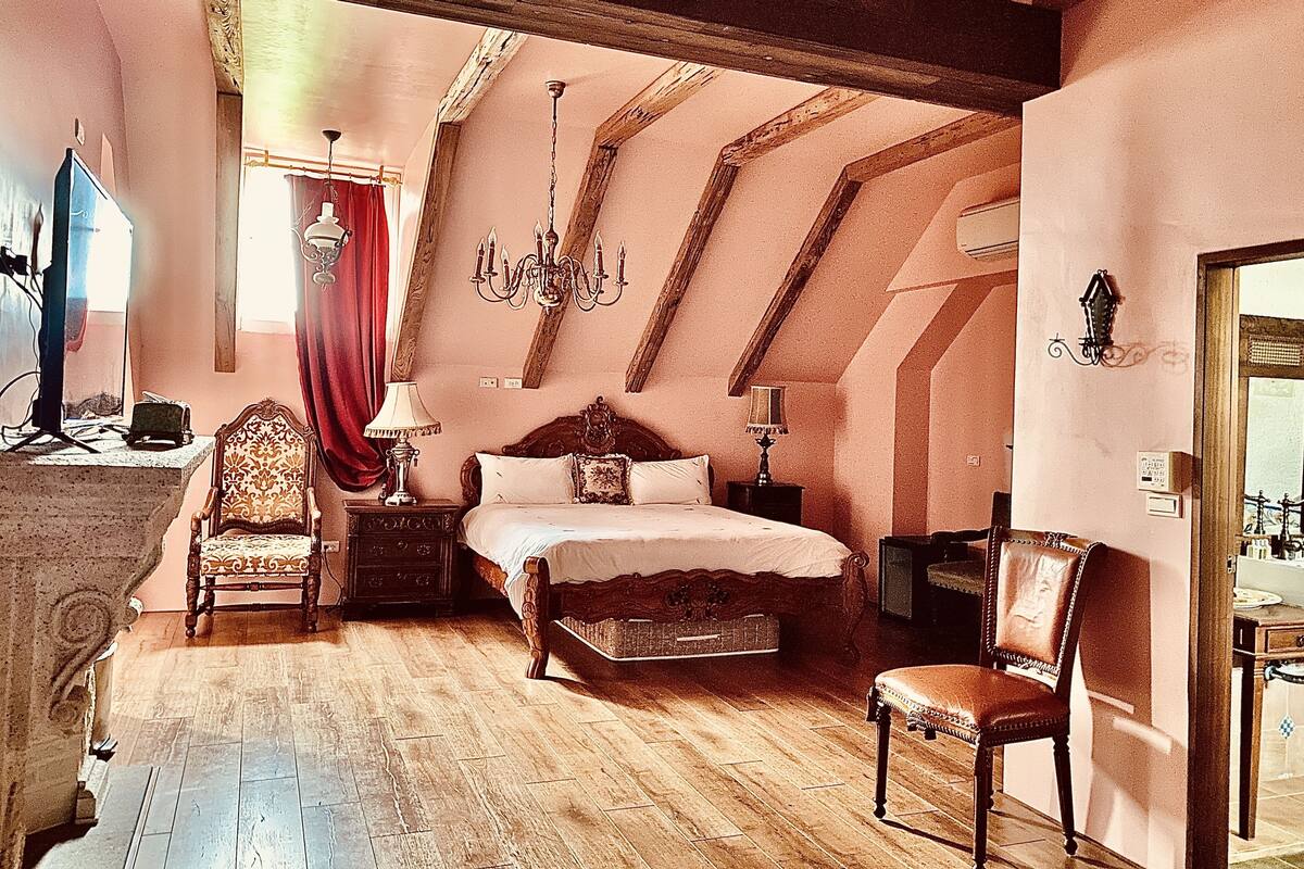 Quarto com teto de madeira, uma cama grande, um candelabro e uma cadeira.