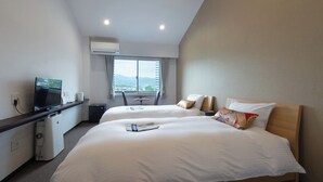 Quarto de hotel com duas camas, uma escrivaninha com televisão e uma janela com vista para as montanhas.