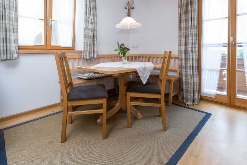 Uma área de refeições com uma mesa e cadeiras de madeira, um vaso com flores e uma janela com cortinas.