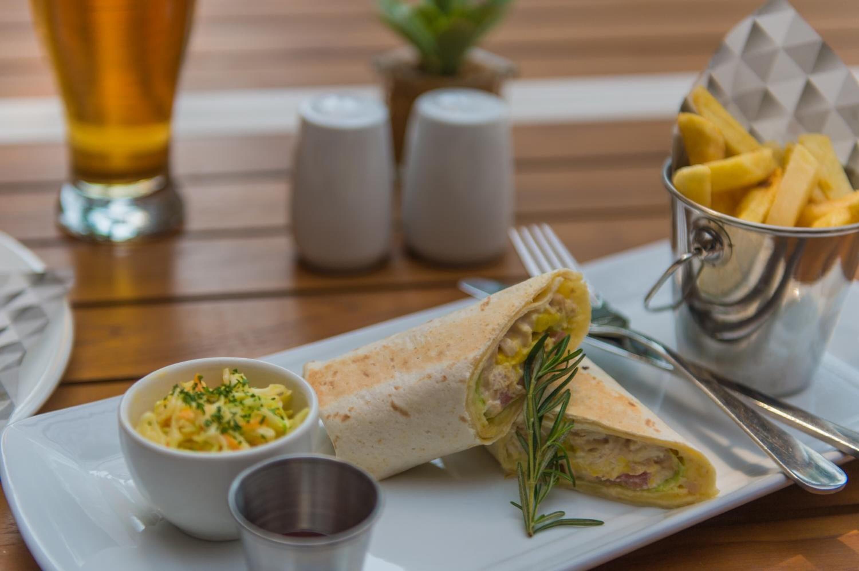 Um prato com um wrap, uma tigela pequena de salada de repolho e um recipiente com batatas fritas.