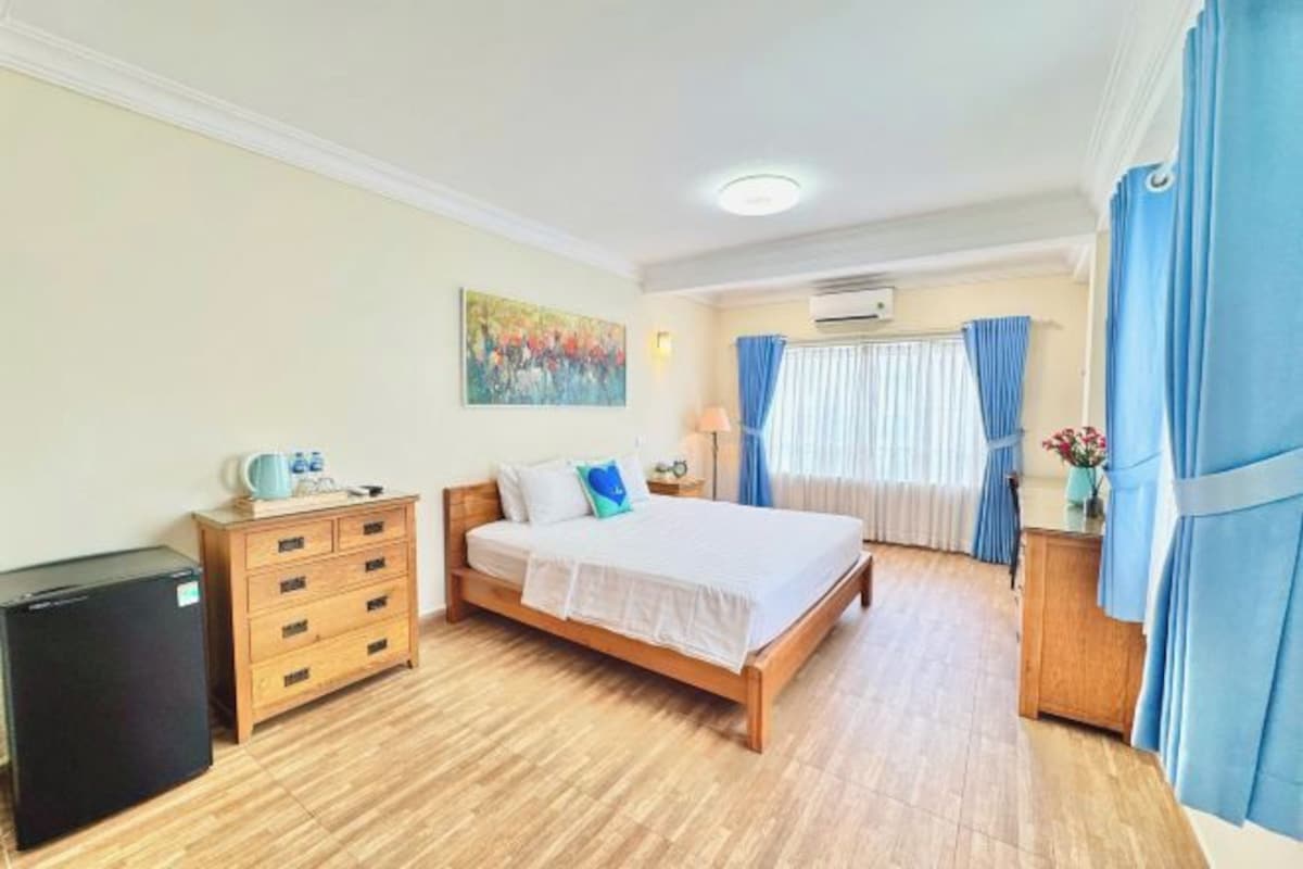 Quarto com cama, cómoda de madeira e um pequeno frigorífico preto.