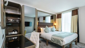 Quarto de hotel com cama, mesa de cabeceira e escrivaninha embutida com espelho.