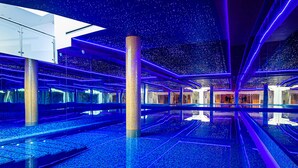 Piscina interior moderna com teto estrelado e iluminação azul.