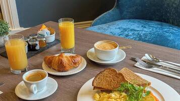 Mesa de café da manhã com croissants, torradas, ovos mexidos, salmão defumado e salada de frutas.