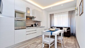 Uma cozinha moderna com eletrodomésticos embutidos, um espaço de refeições com mesa e cadeiras, e um sofá na sala adjacente.
