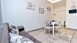 Uma sala de estar moderna com um sofá cinzento, uma mesa de jantar com cadeiras e um tapete estampado.