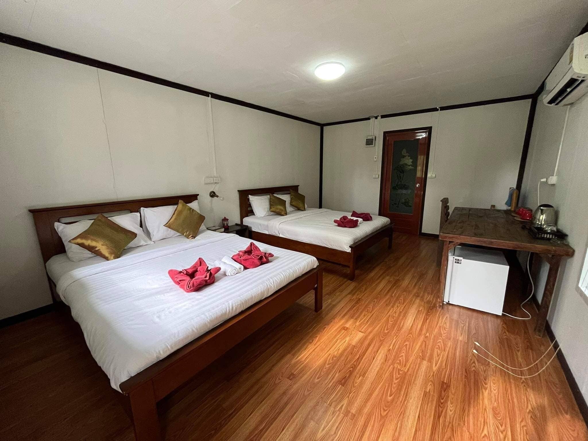 Quarto de hotel com duas camas de madeira, roupa de cama branca e toalhas vermelhas.