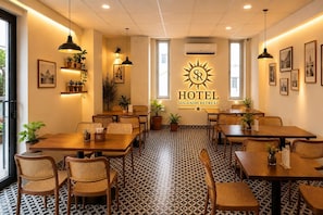 Interior de hotel com várias mesas e cadeiras para refeições, piso estampado e parede central com logotipo e nome.