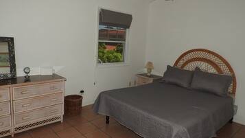 Quarto com cama, cômoda e janela com vista para o verde.