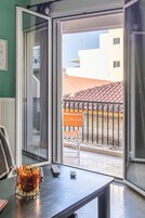 Quarto com varanda, uma mesa com vela e vista para prédios e um telhado telhado.