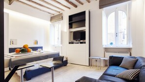 Cozinha moderna com forno embutido, área de jantar com mesa e cadeiras, e sala de estar com sofá e janela.