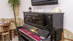 Um piano de cauda preto num aposento com parede de pedra, uma televisão acima e um telefone sobre o piano.
