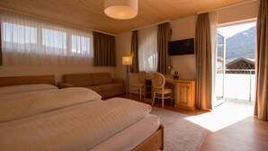 Quarto de hotel com uma cama grande, uma escrivaninha, uma cadeira e uma televisão.