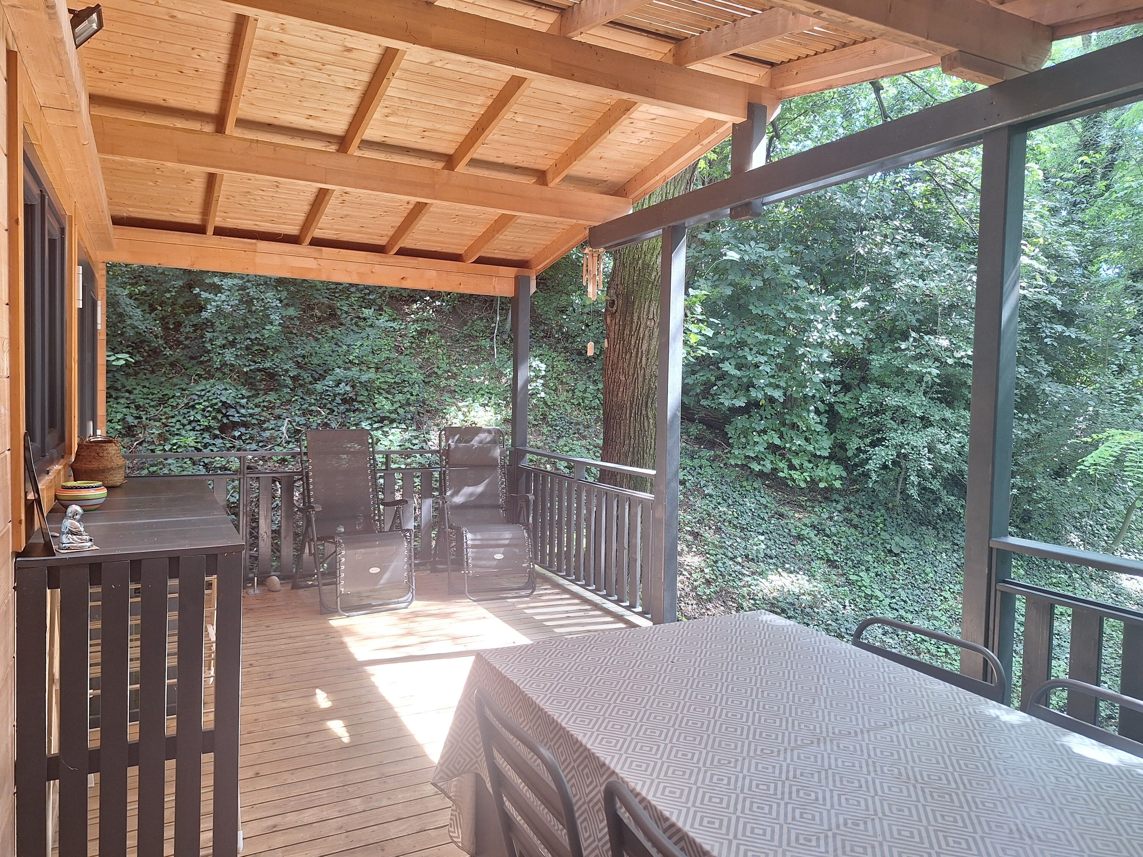 Um deck de madeira com mesa e cadeiras, cercado por uma grade, com vista para uma área arborizada.