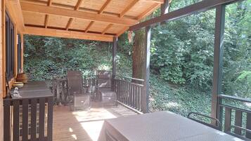 Um deck de madeira com mesa e cadeiras, cercado por uma grade, com vista para uma área arborizada.