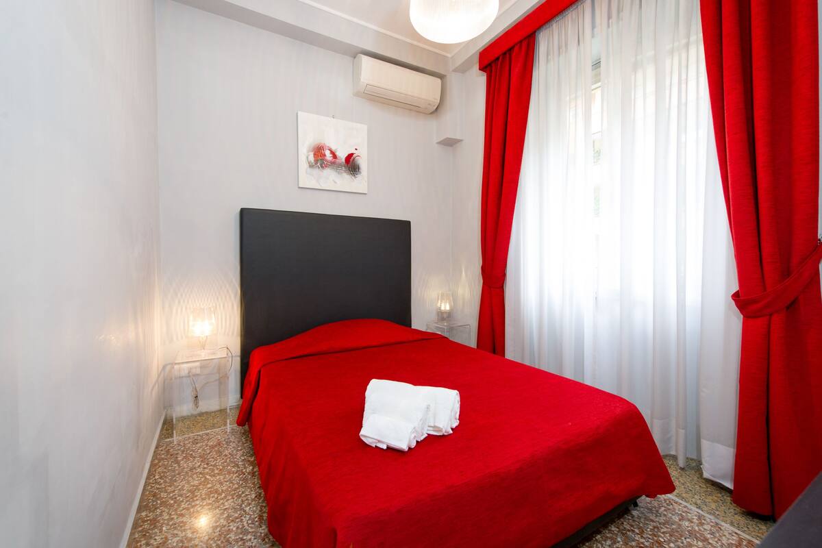 Quarto de hotel com cama, mesa de cabeceira, luminária e ar condicionado fixado na parede.