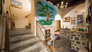Uma escadaria com degraus de pedra e corrimão de metal, que leva a um quarto com parede de pedra e um mural de uma árvore.