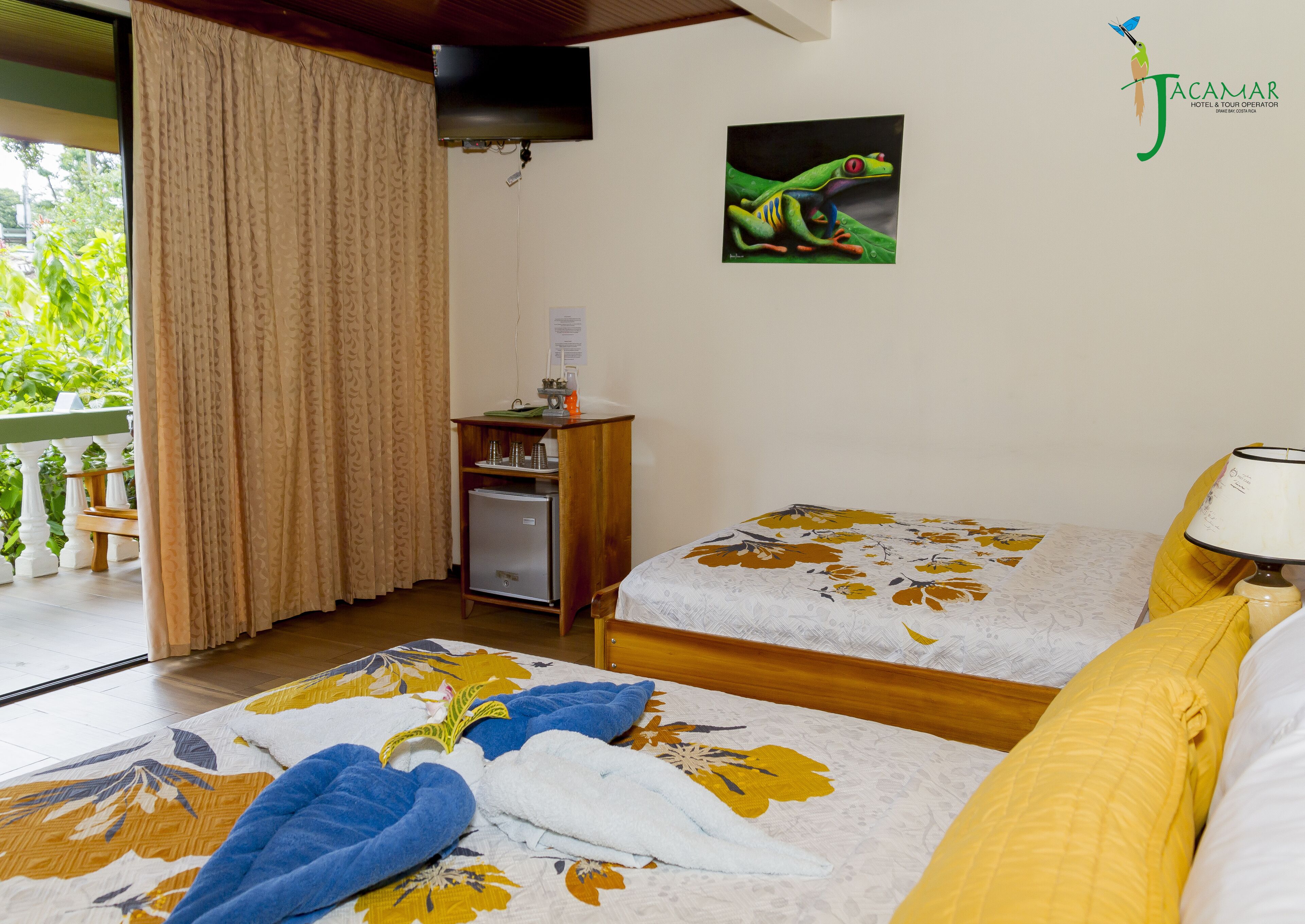 Quarto de hotel com duas camas, uma escrivaninha, uma televisão e uma janela com cortinas.