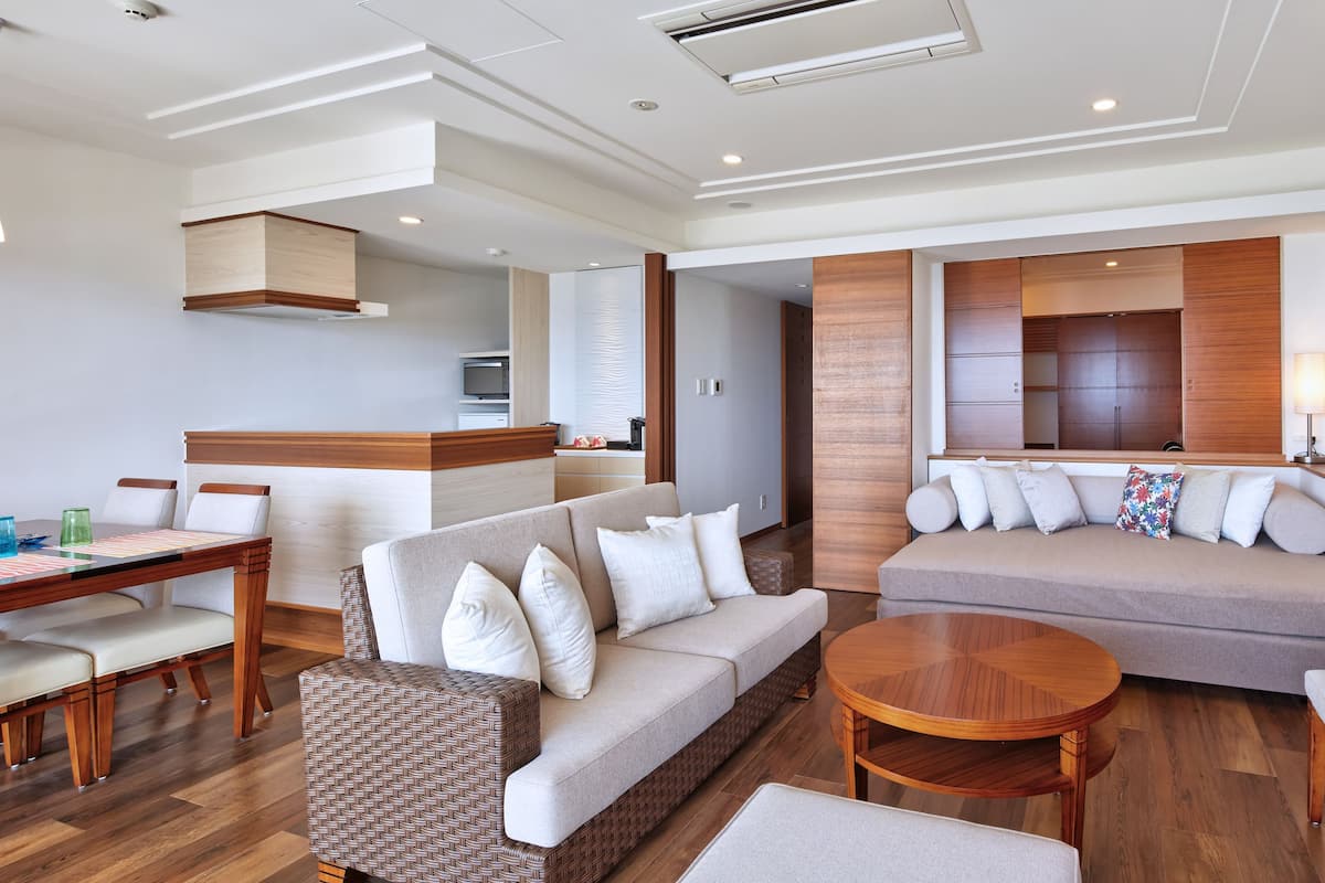 Quarto de hotel moderno com área de refeições, sofá, televisão e piso de madeira.