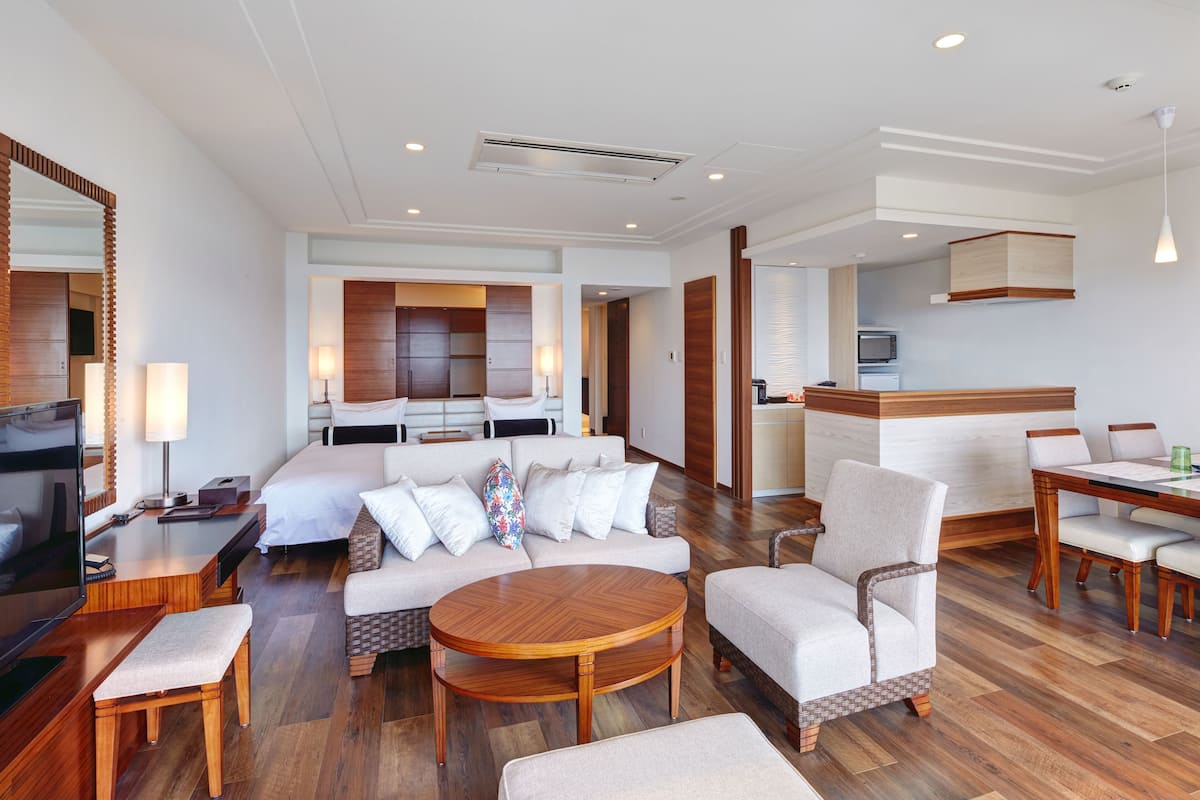 Quarto de hotel com cama, sofá, mesa de jantar, cadeiras e televisão.