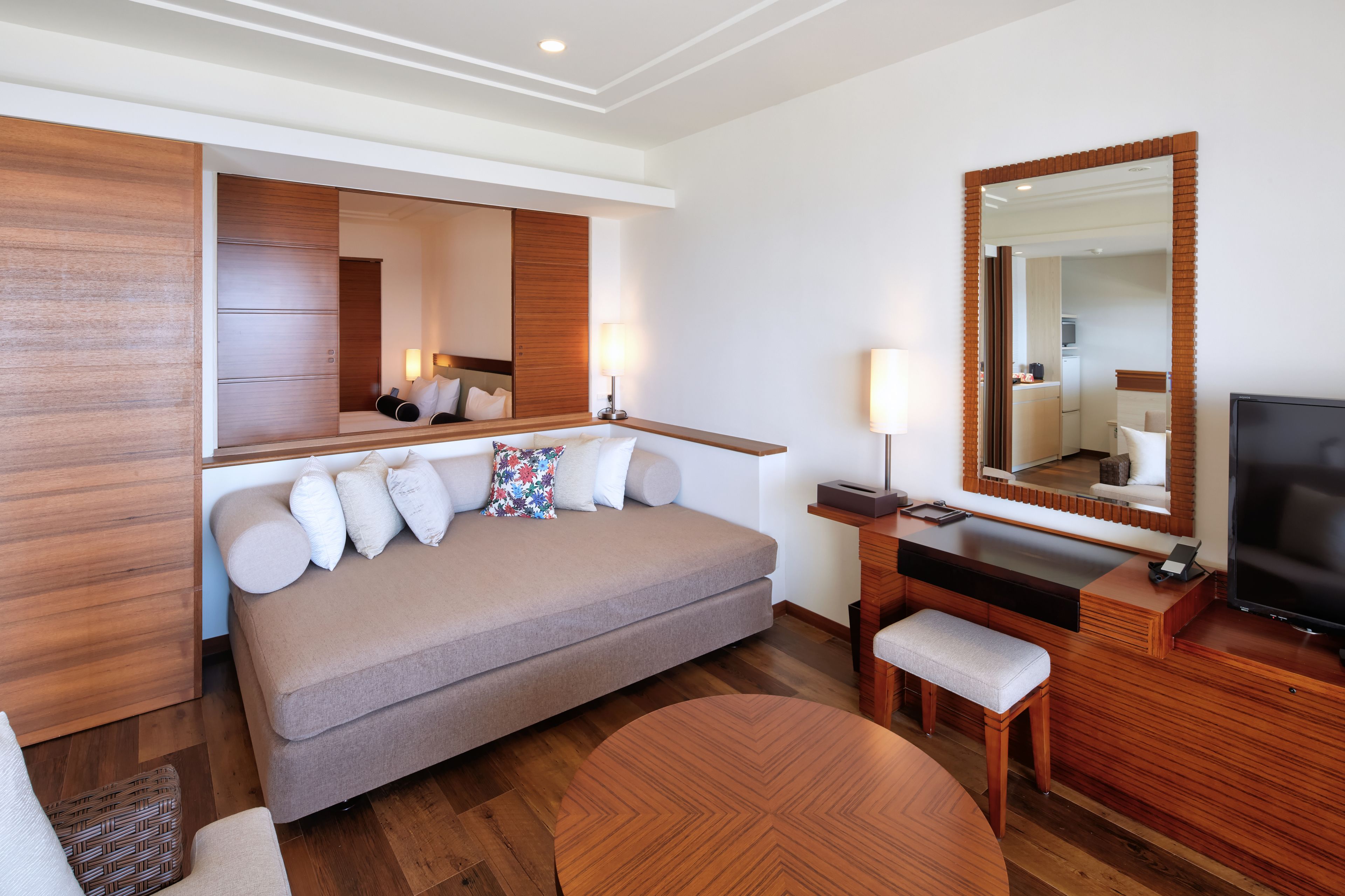 Quarto de hotel moderno com sofá, escrivaninha de madeira, televisão e um espelho grande.