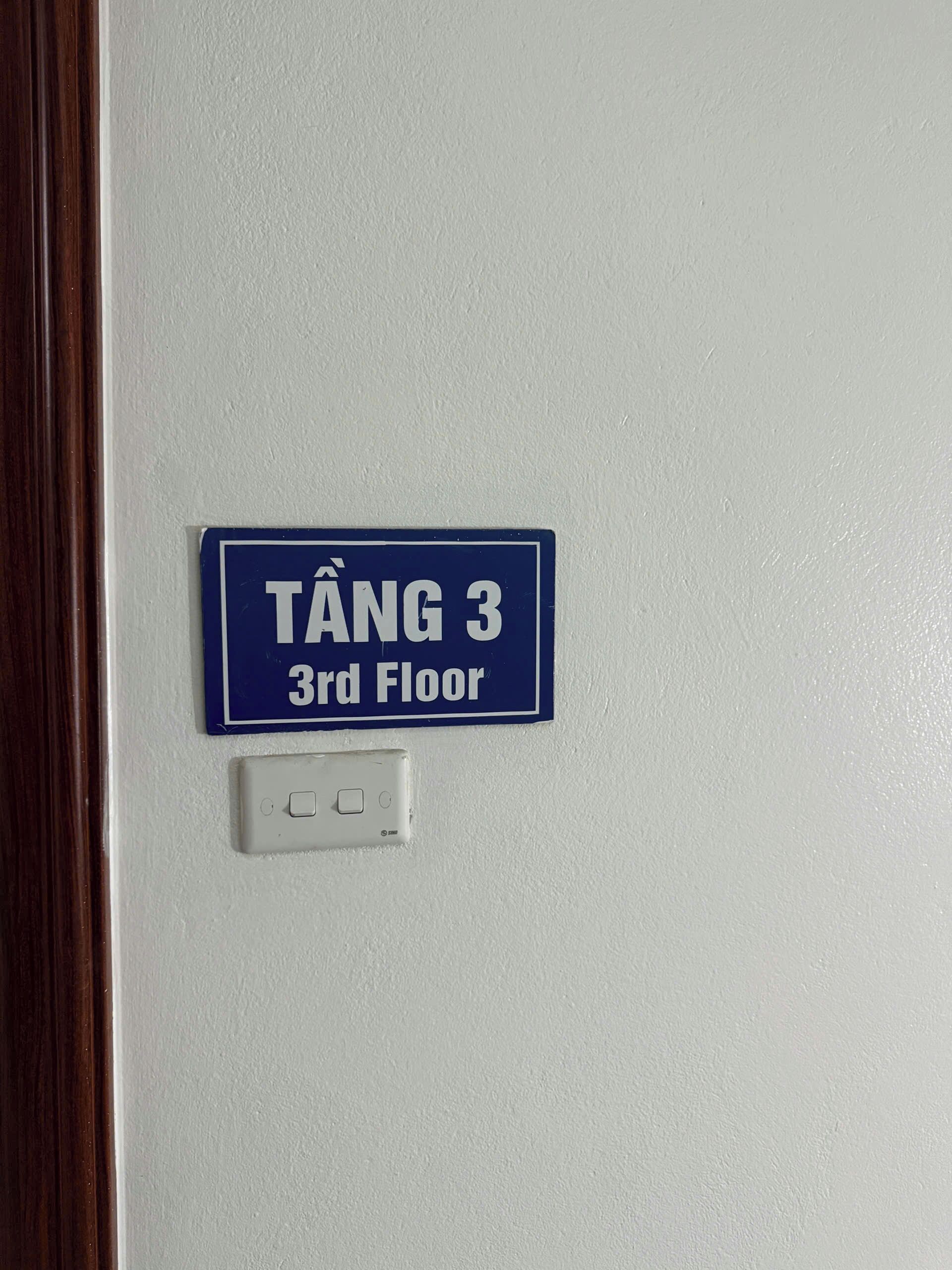 Um sinal azul com texto branco indicando 'TÂNG 3 3º Andar' acima de um interruptor elétrico branco.
