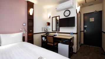 Quarto de hotel com cama, escrivaninha, cadeira e relógio na parede.