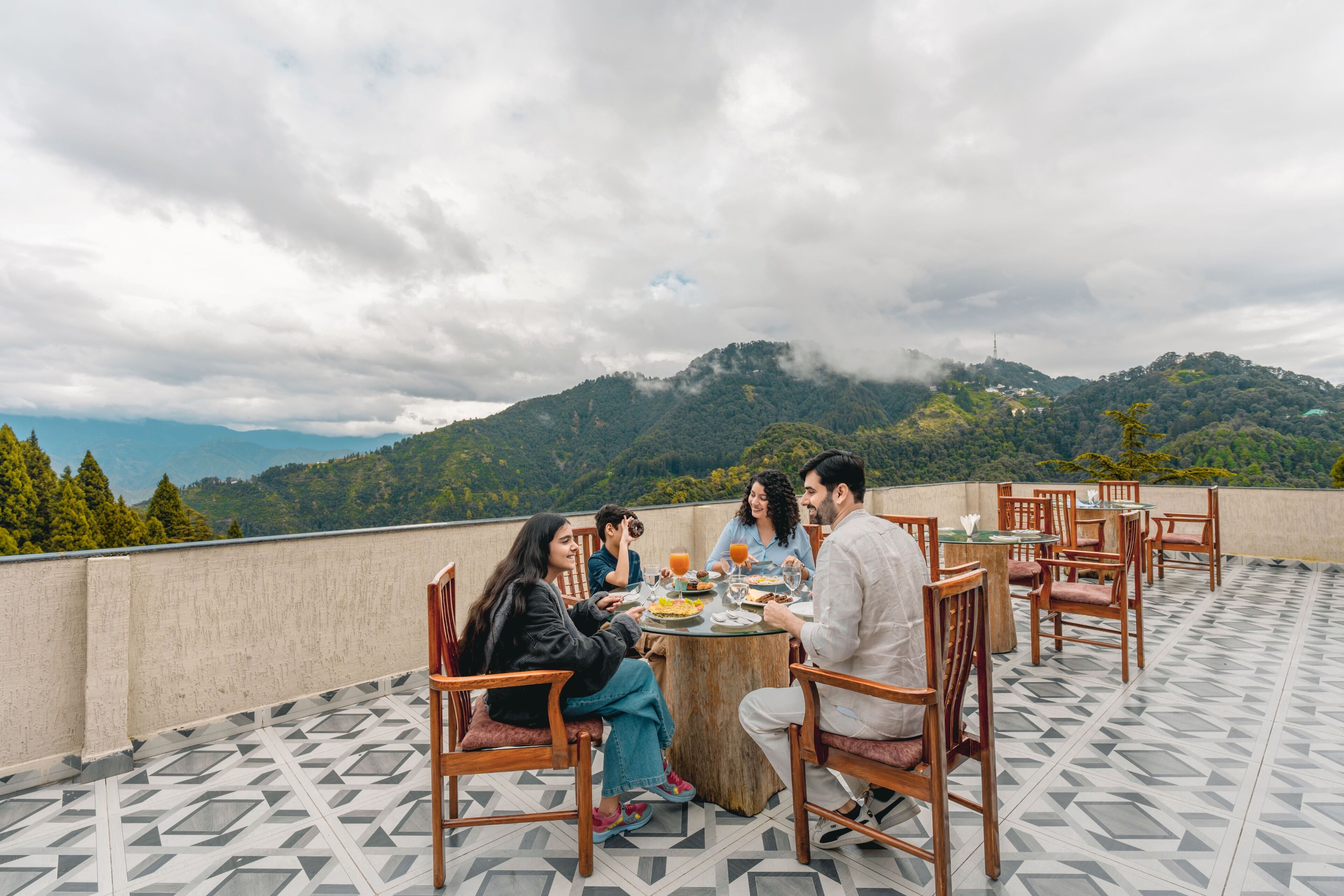 Um grupo de pessoas jantando em um terraço no topo de um prédio, com montanhas ao fundo.