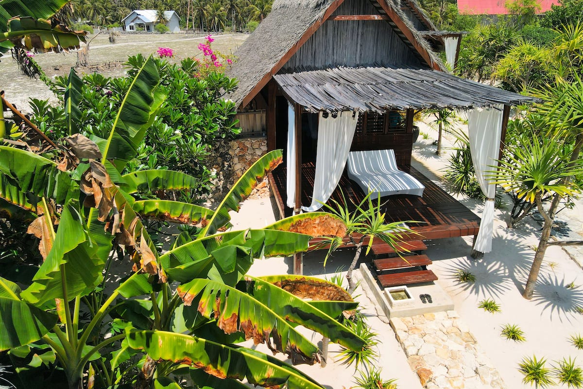 Uma cabana com telhado de palha, deck de madeira e cortina branca.