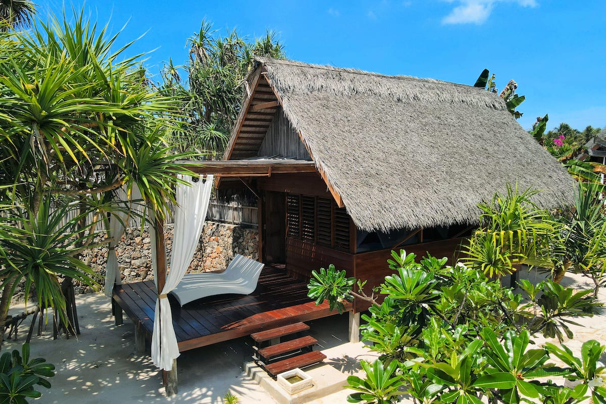 Uma cabana com telhado de palha, um deck de madeira e uma parede de pedra.