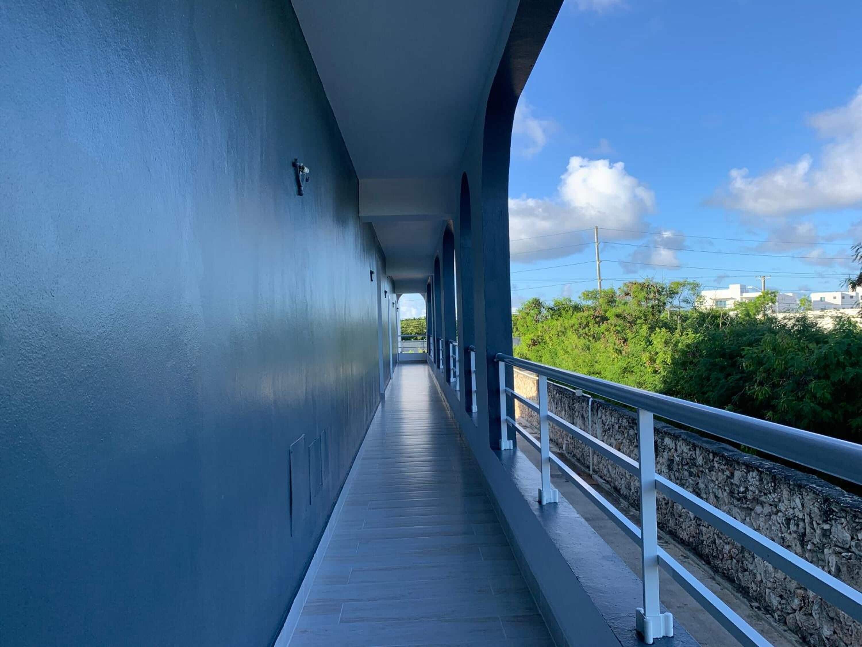 Galeria coberta em navio de cruzeiro, com vista para áreas verdes e edifícios ao longe.