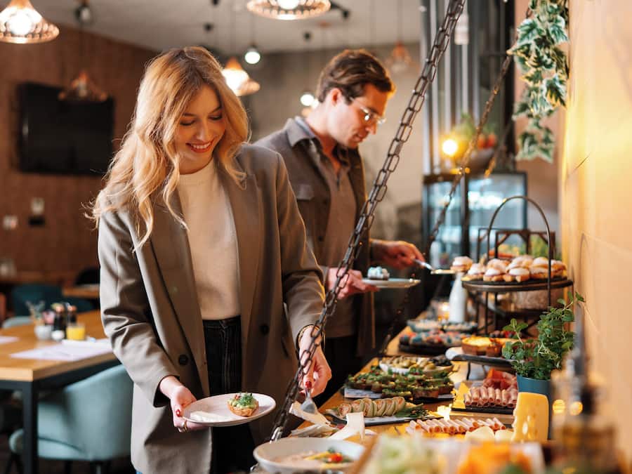 Disposição de buffet com diversos alimentos e uma pessoa servindo.