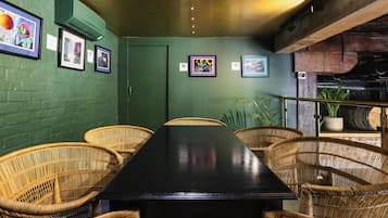 Um quarto com uma mesa preta alongada, rodeada por cadeiras de vime, paredes verdes e quadros decorativos.
