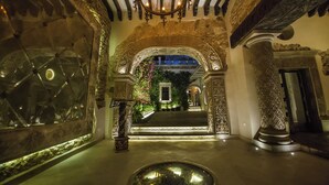 Um corredor ornamentado com um candelabro, colunas e uma parede de vidro com padrão geométrico.