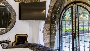 Quarto com parede de pedra, uma cama grande, televisão na parede e um candeeiro decorativo.